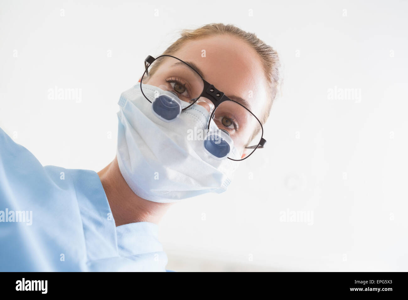 Dentist in surgical mask and dental loupes looking down over patient ...