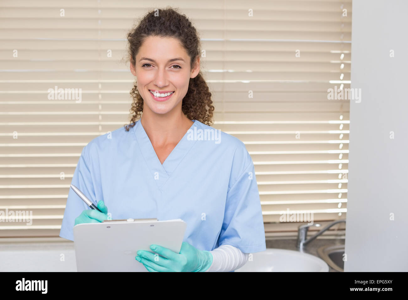 Dentist in blue scrubs writing on clipboard Stock Photo - Alamy