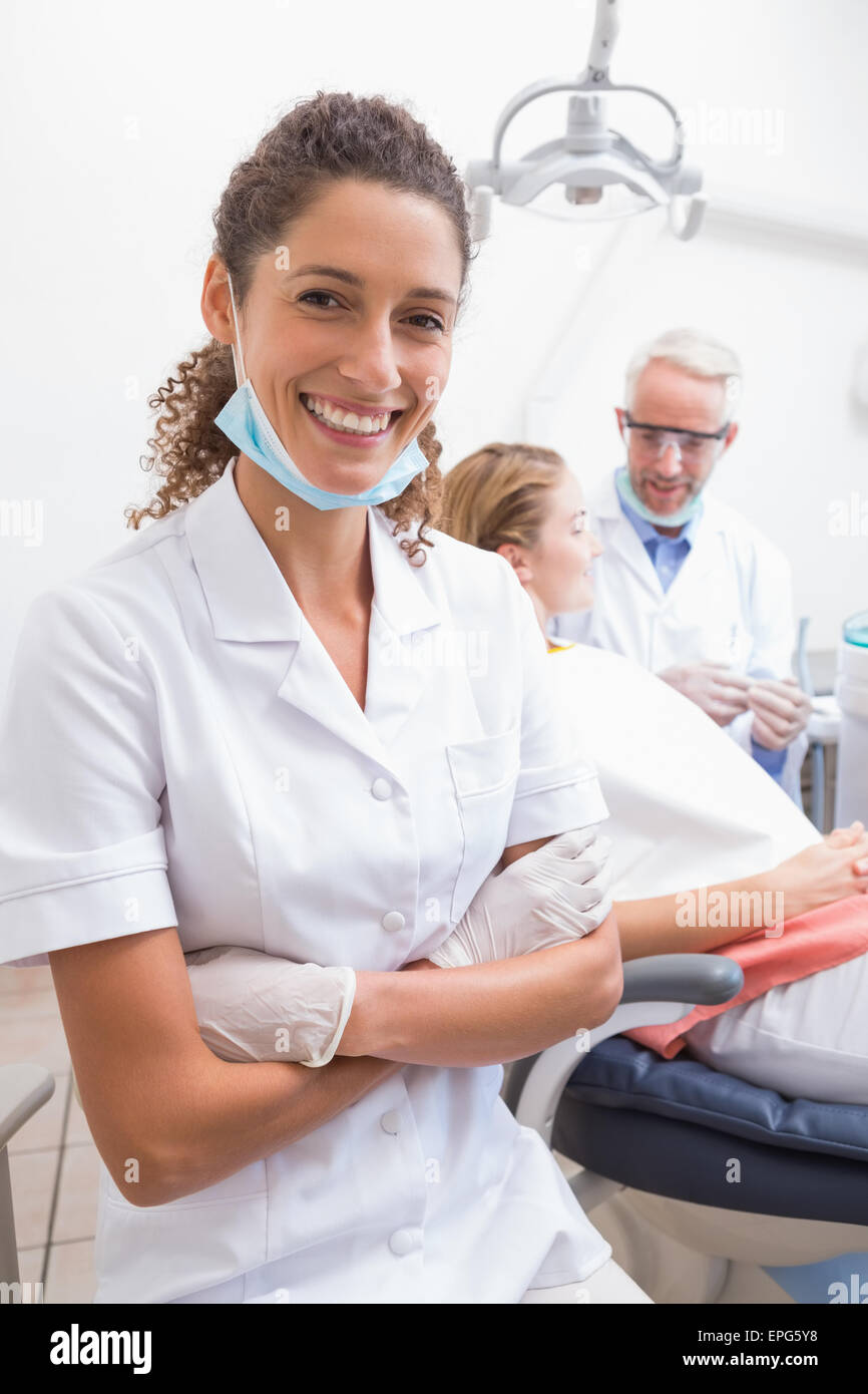 Dental assistant smiling at camera with dentist and patient behind ...