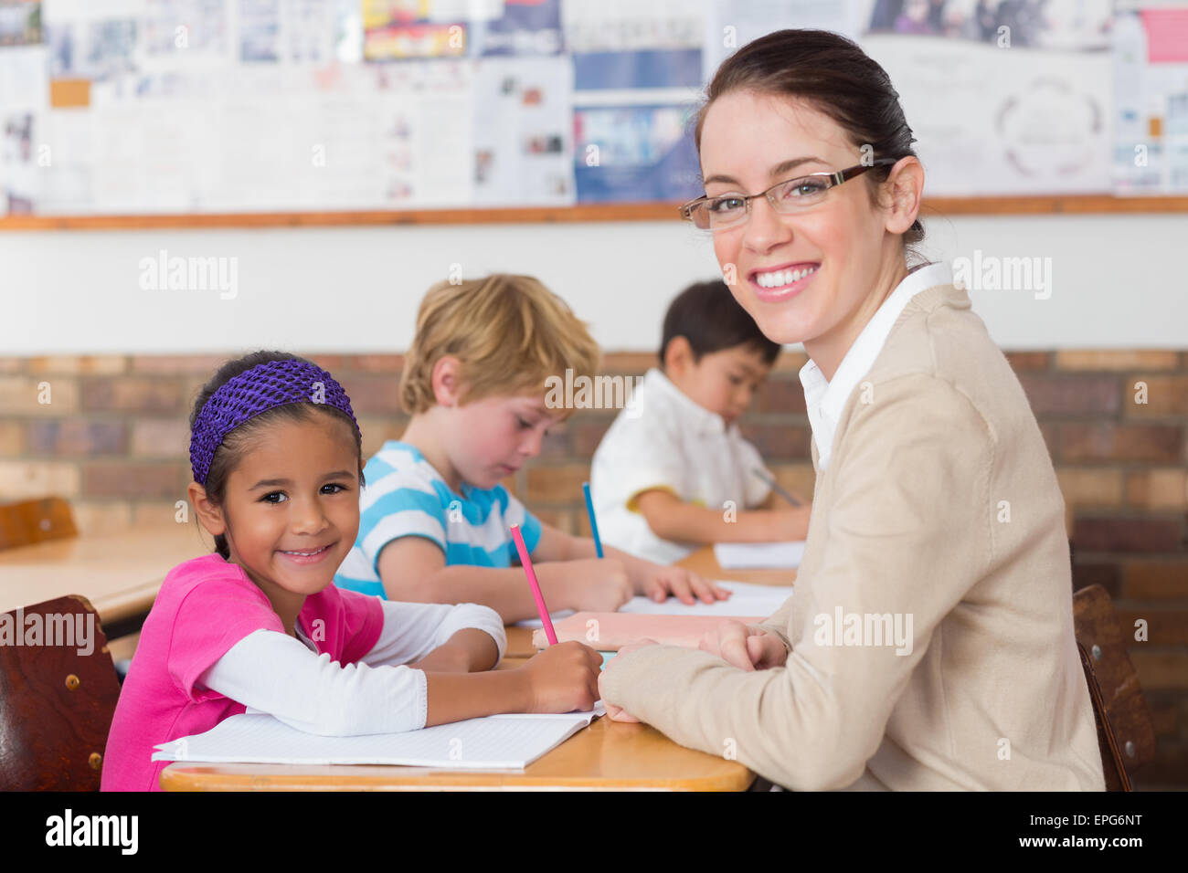 Pretty teacher helping pupil in classroom smiling at camera Stock Photo ...