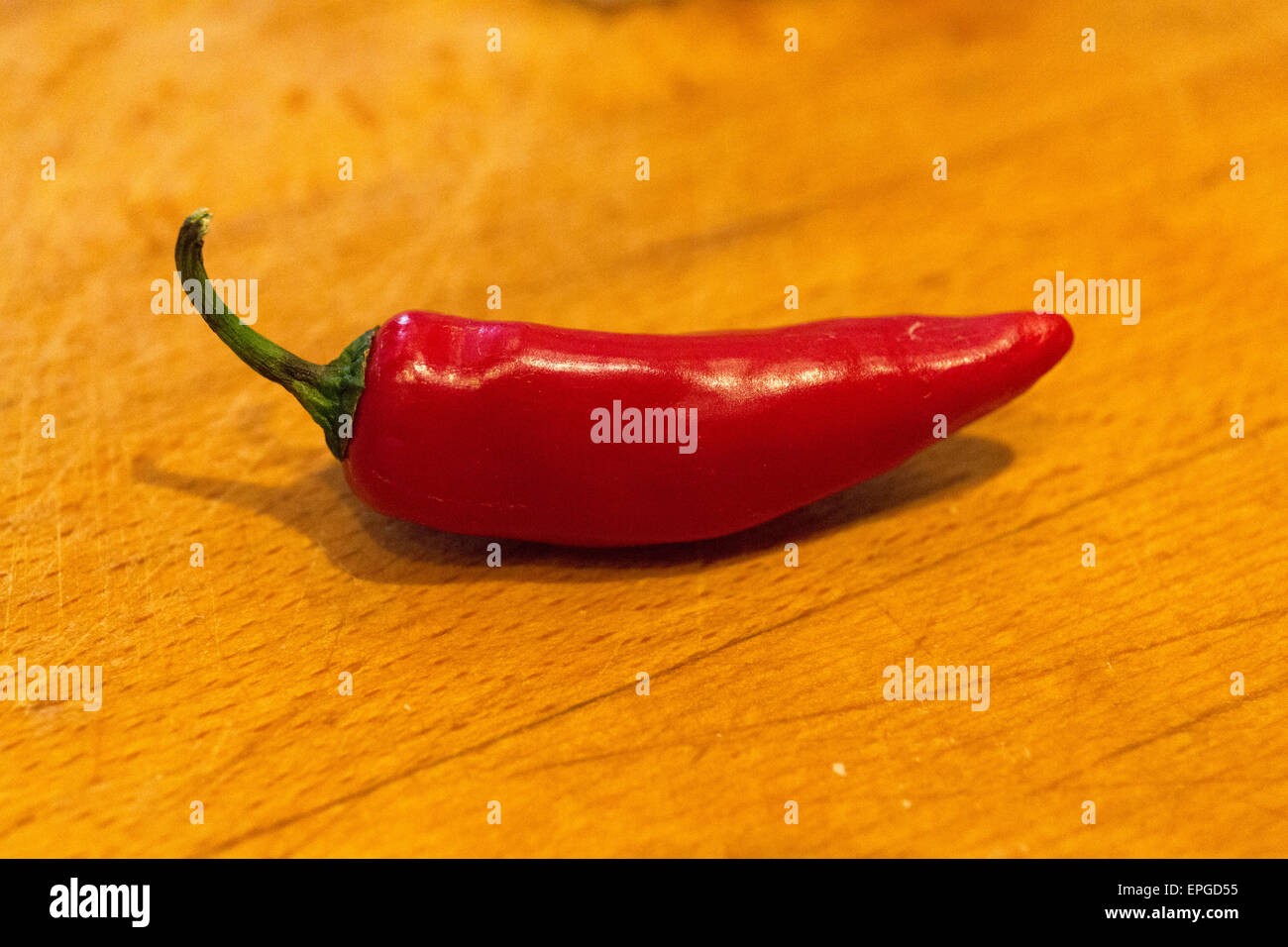 A whole red chilli pepper on a wooden chopping board Stock Photo - Alamy