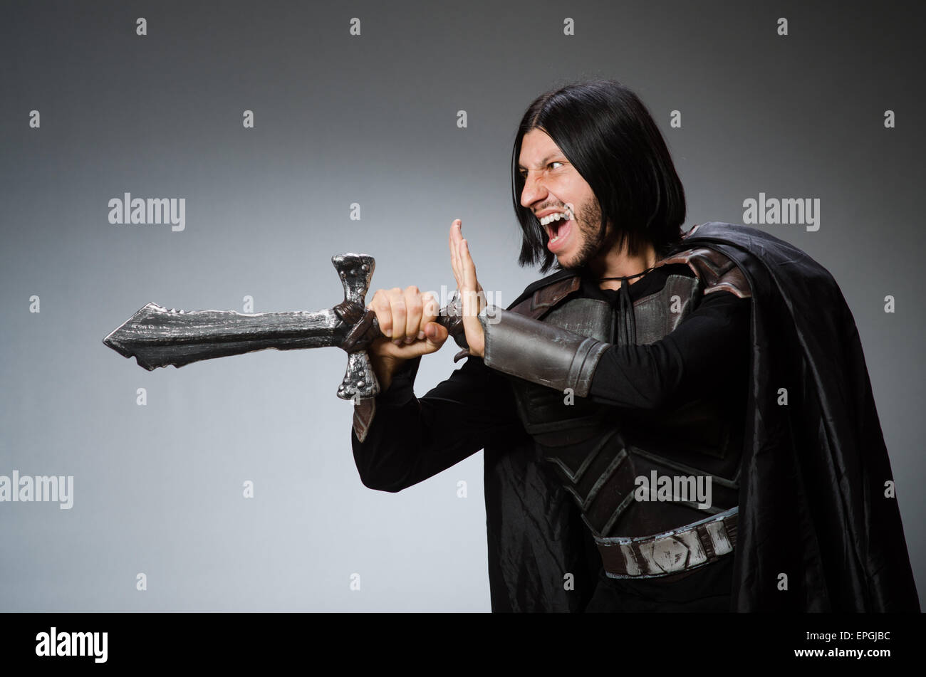 Angry knight with sword against dark background Stock Photo - Alamy