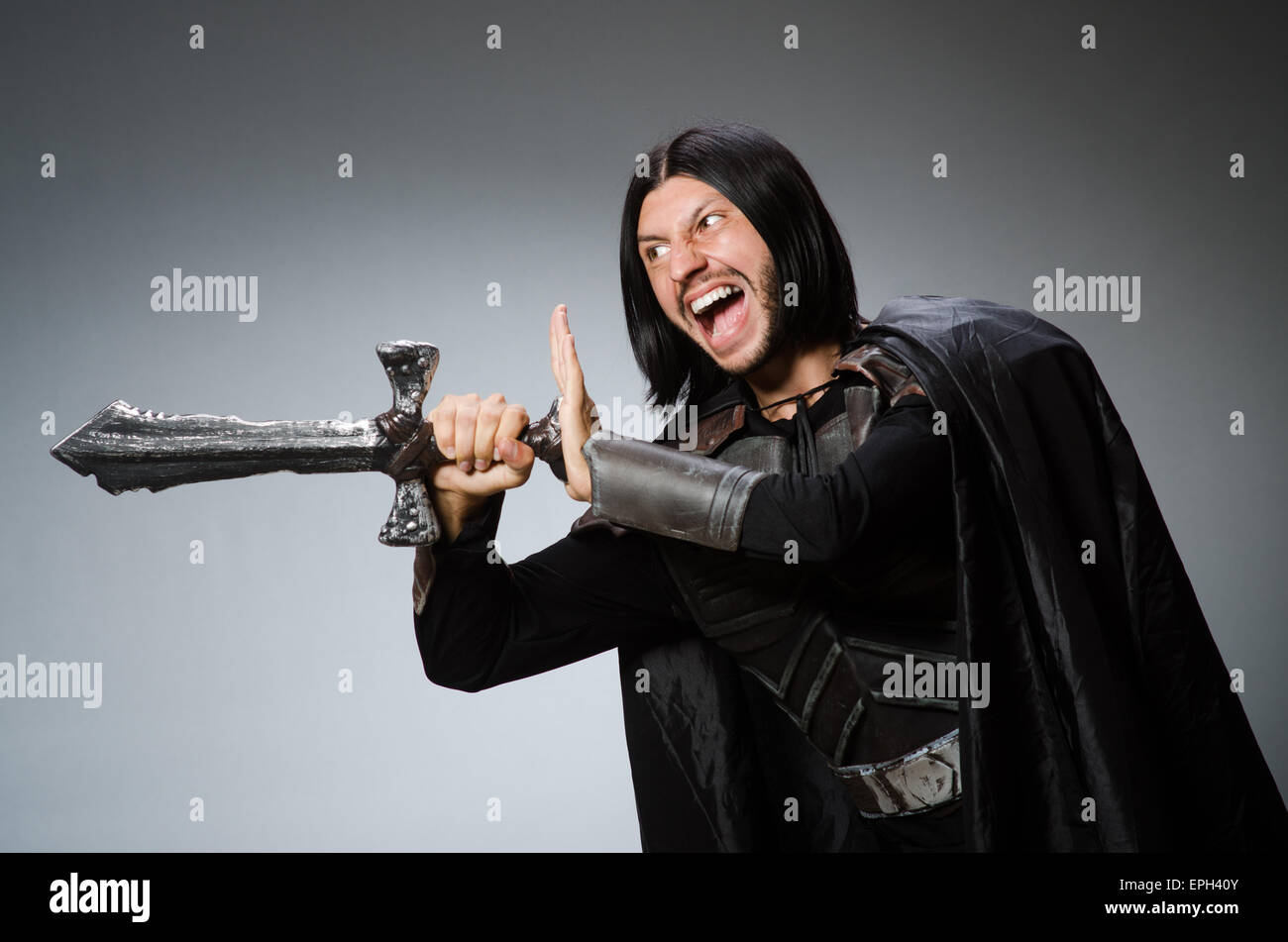 Angry knight with sword against dark background Stock Photo - Alamy