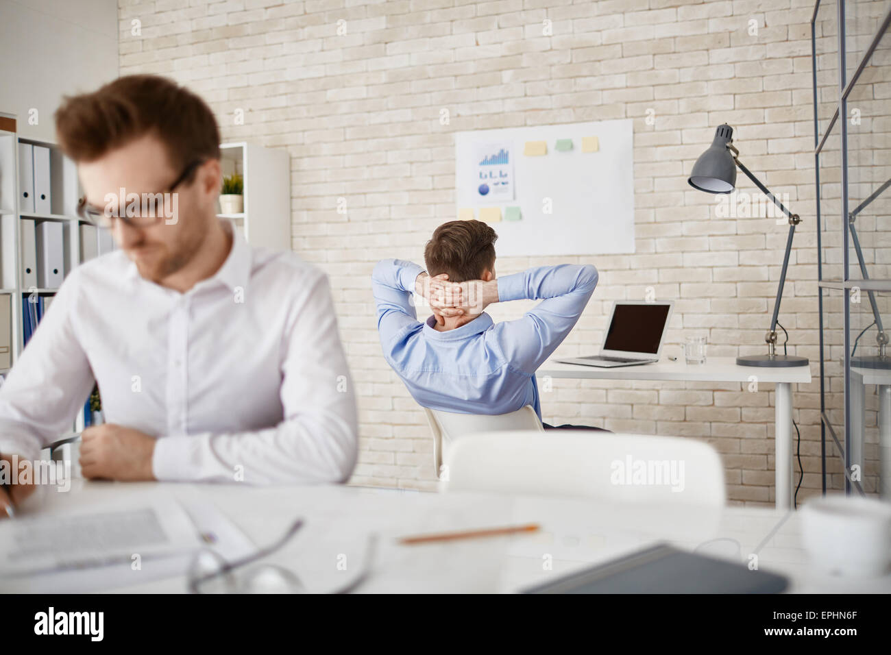 Rear view of restful young businessman sitting by workplace in working ...