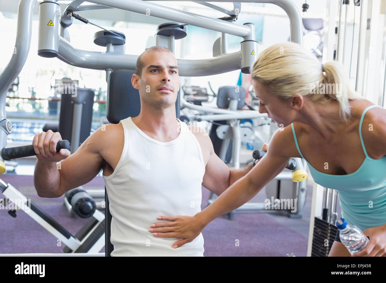 Trainer assisting man on fitness machine at gym Stock Photo - Alamy