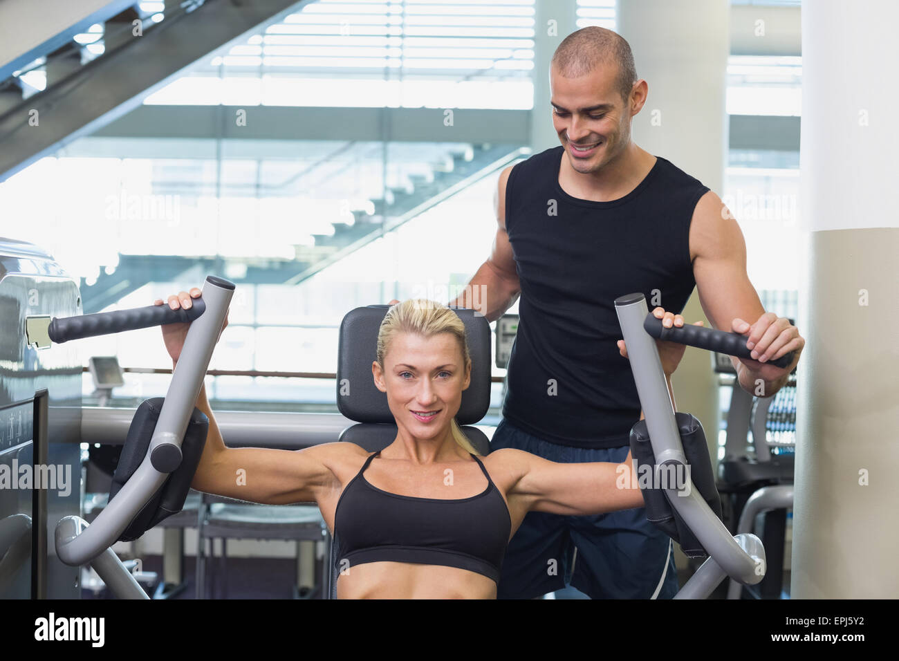 Trainer assisting woman on fitness machine at gym Stock Photo - Alamy