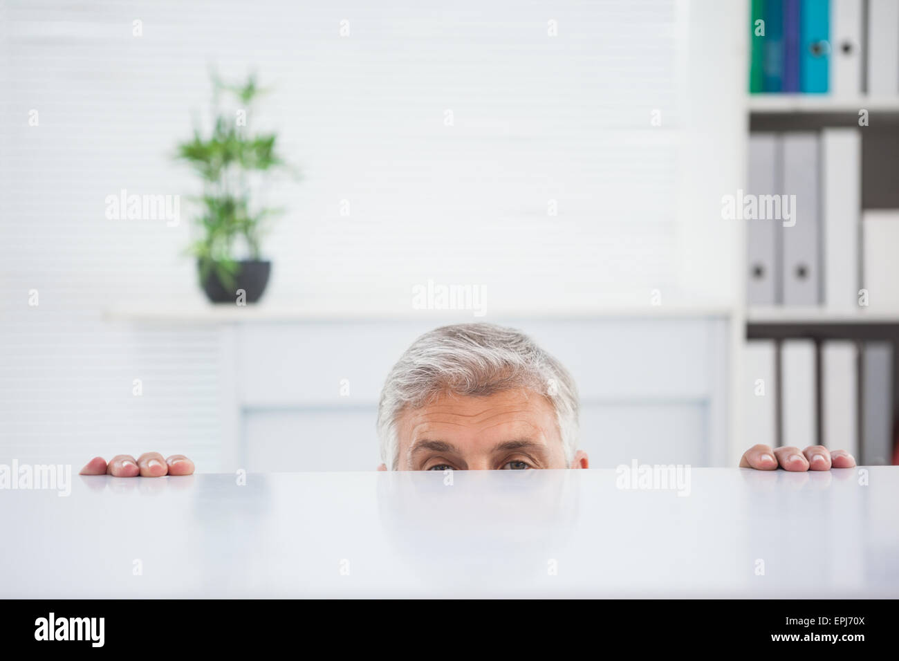 Nervous businessman peeking over desk Stock Photo - Alamy