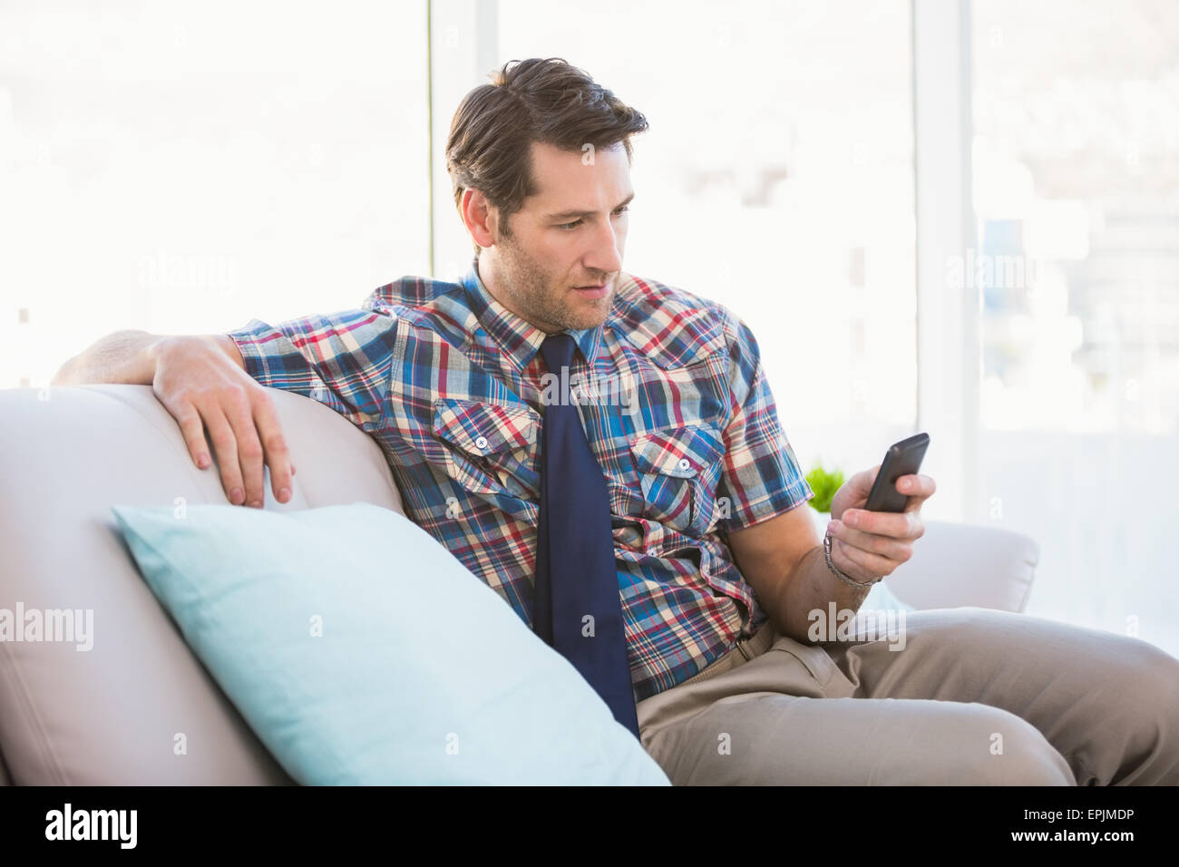 Happy man sitting on the couch sending a text message Stock Photo - Alamy