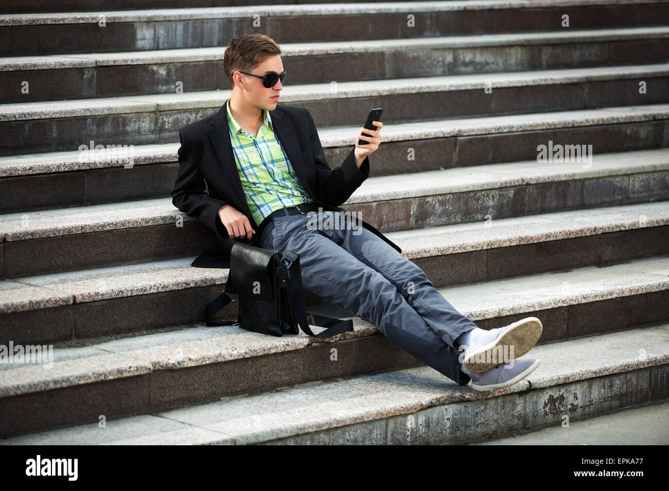 Young man with a mobile phone sitting on the steps Stock Photo - Alamy