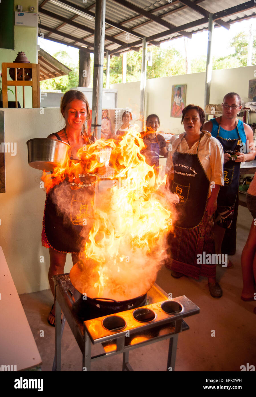 A woman pours water into hot oil in a pan creating large fire during in ...