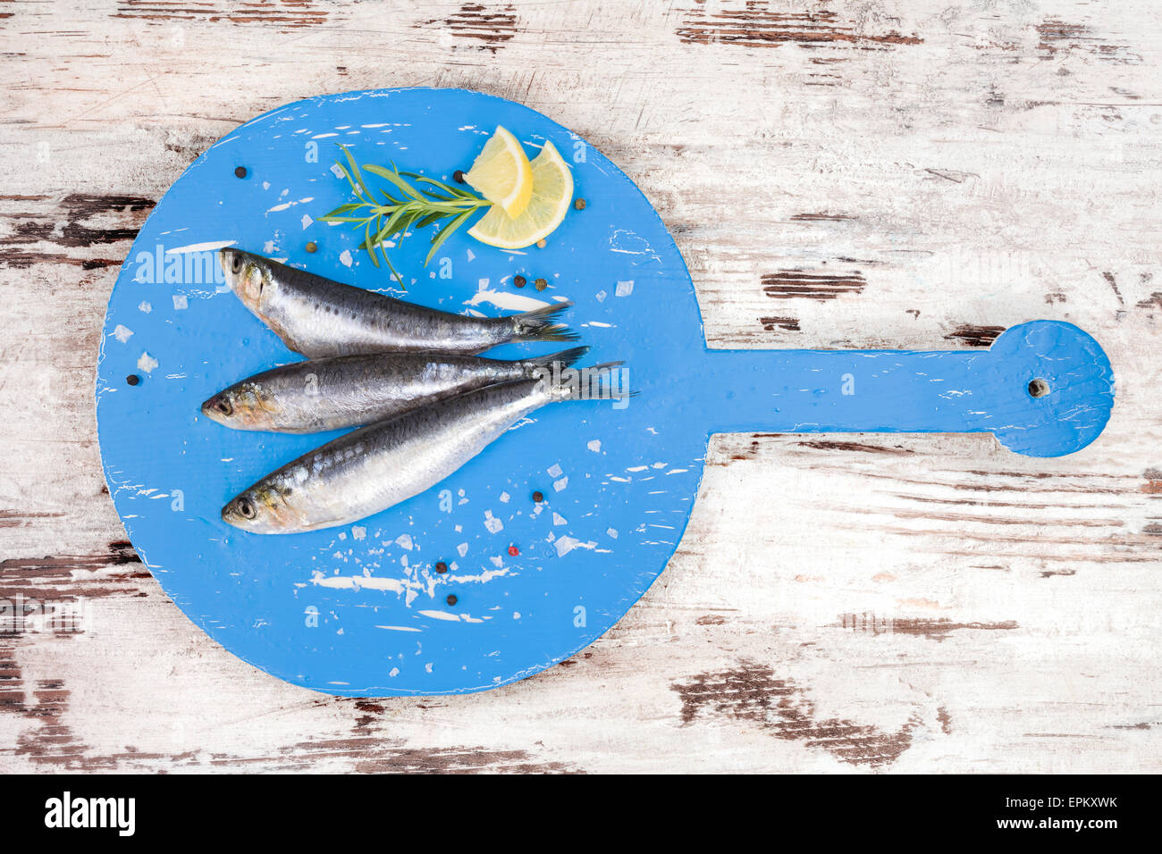 Three fresh anchovy fish on round blue wooden kitchen board on white ...