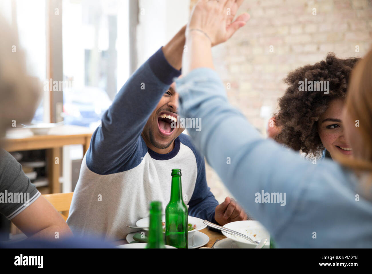 Happy friends at dining table with beer bottles high fiving Stock Photo ...