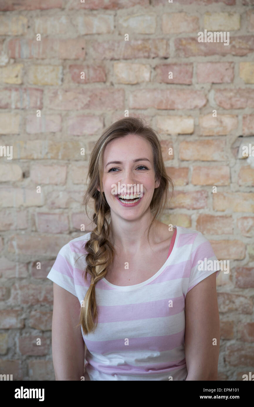 Portrait of laughing young woman in front of brick wall Stock Photo - Alamy