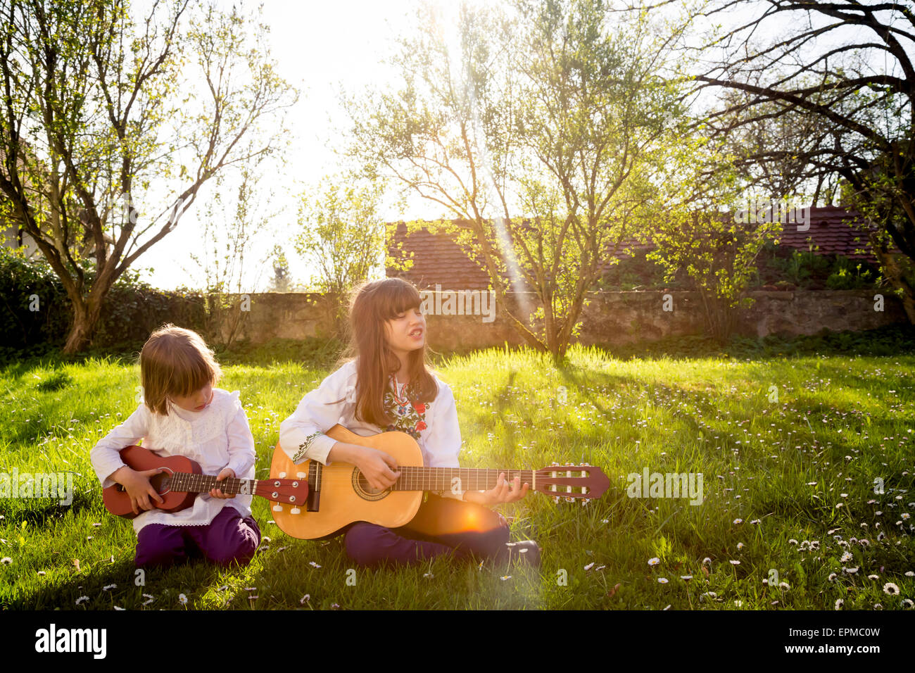 Two sisters sitting on a meadow playing guitar Stock Photo - Alamy