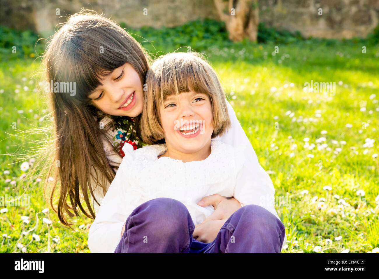 Two sisters sitting together on a meadow in the garden Stock Photo - Alamy