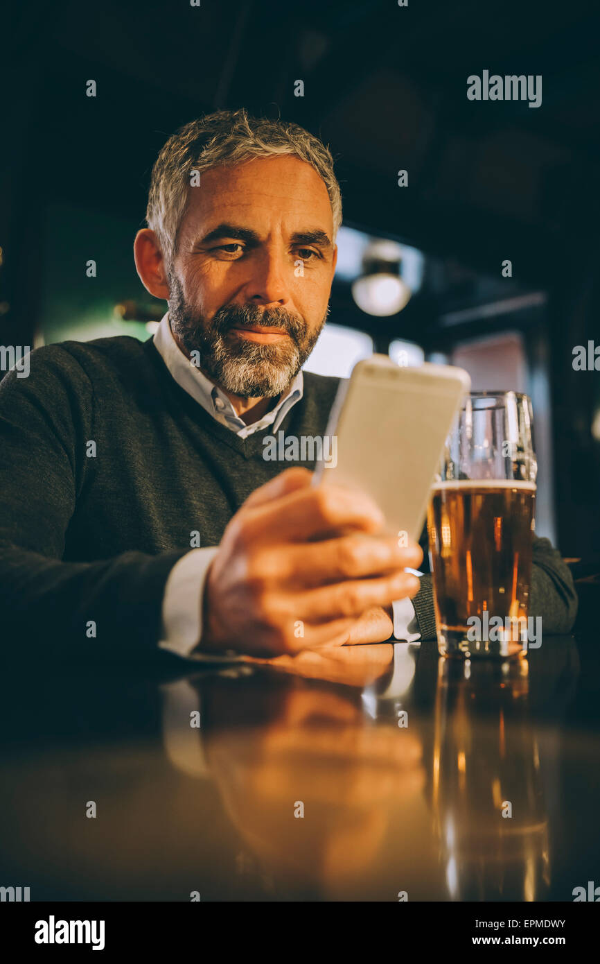 Man sitting at counter of a pub looking at his smartphone Stock Photo ...