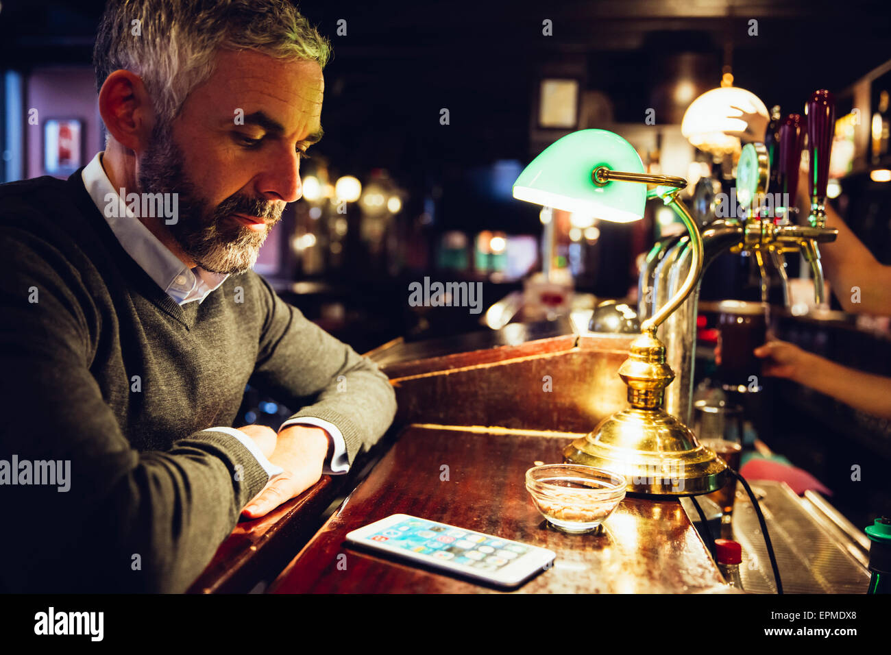 Man sitting at counter of a pub looking at his smartphone Stock Photo ...