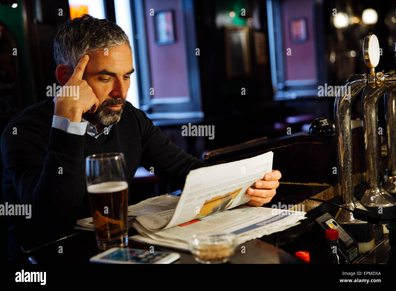 Man sitting at counter of a pub reading newspaper Stock Photo - Alamy