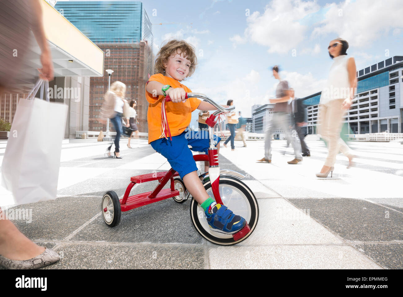 Boy riding a tricycle between a crowd of people in a city Stock Photo ...