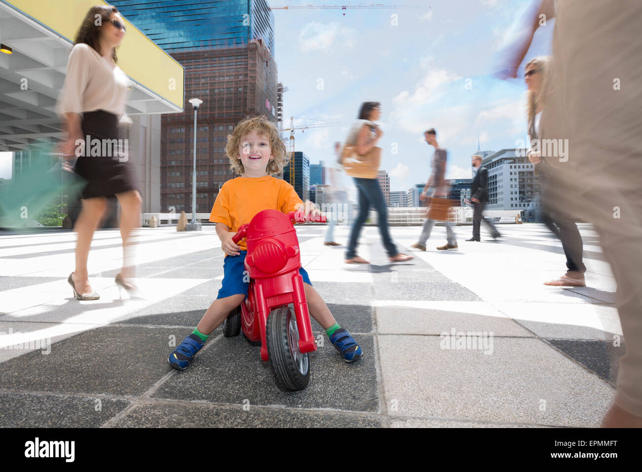 Boy riding a plastic tricycle between a crowd of people in a city Stock ...