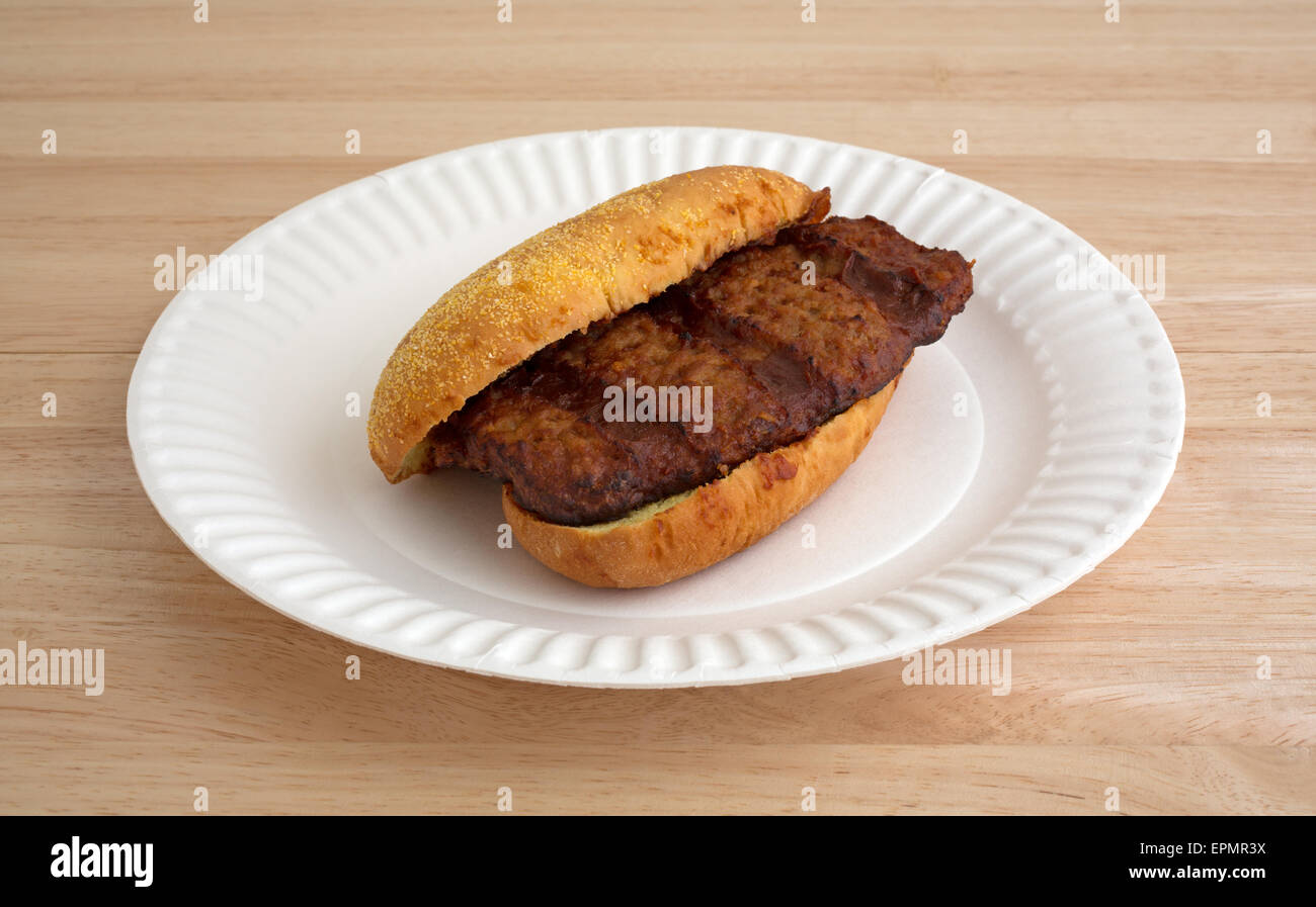 A pork rib sandwich with barbecue sauce on a white paper plate atop a ...