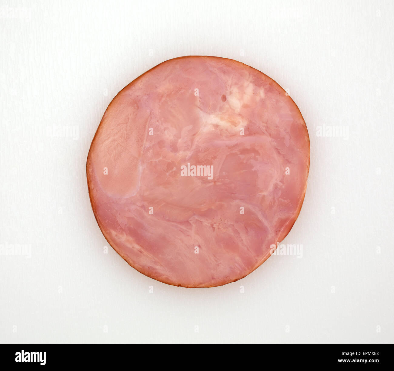 Top view of a round slice of ham on a white cutting board illuminated ...