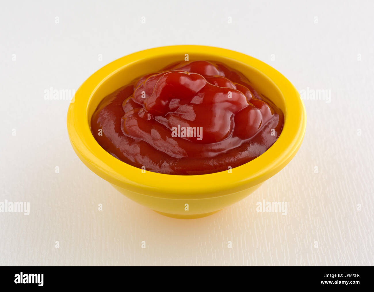 A small yellow portion bowl filled with ketchup on a white cutting ...