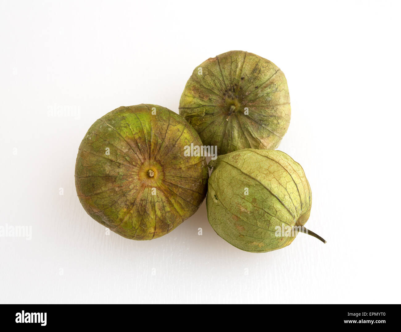 Three ripe tomatillos on a white cutting board illuminated with natural ...