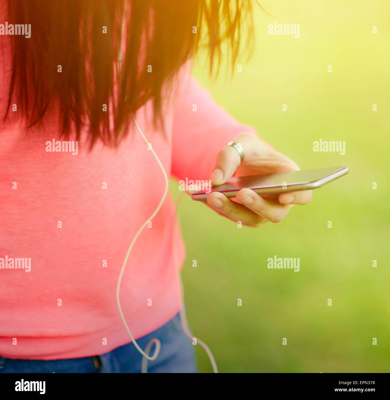 Girls hands holding cell phone while listening to music against green ...
