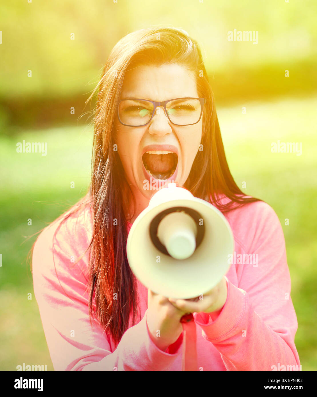 Portrait of middle aged woman shouting using megaphone against a nature ...