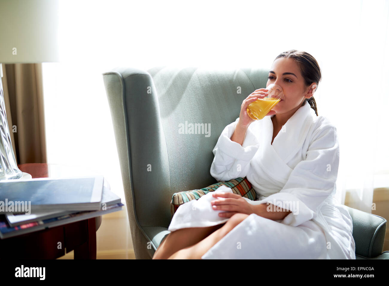 Young woman sitting in wingback chair with legs over chair arms ...