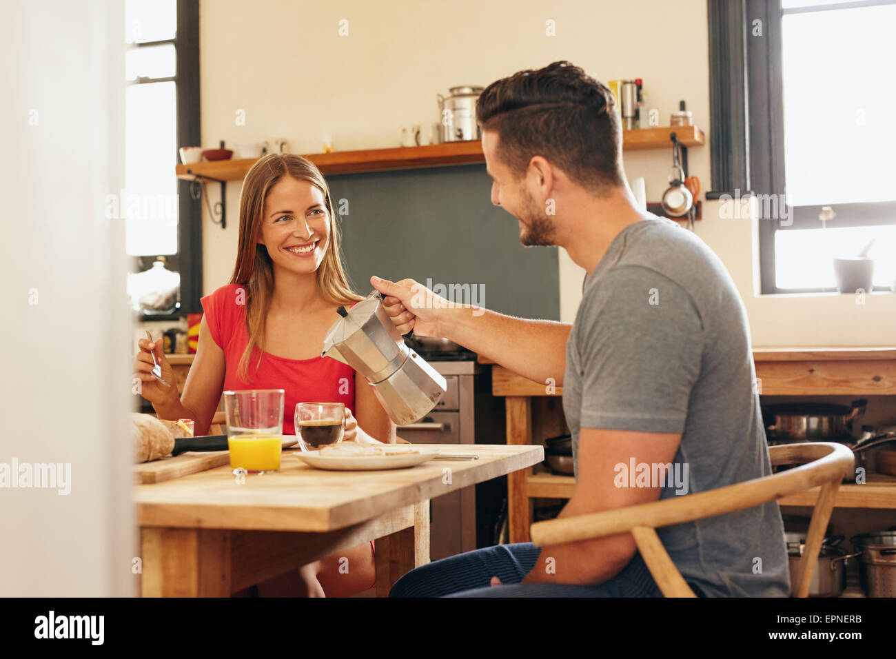 Indoor Shot Of Young Man Serving Coffee To His Girlfriend Having Breakfast In Kitchen At Home