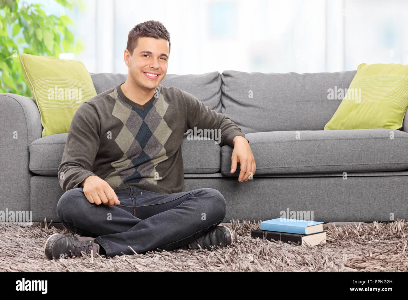 Young relaxed man sitting on the floor at home in front of a modern ...
