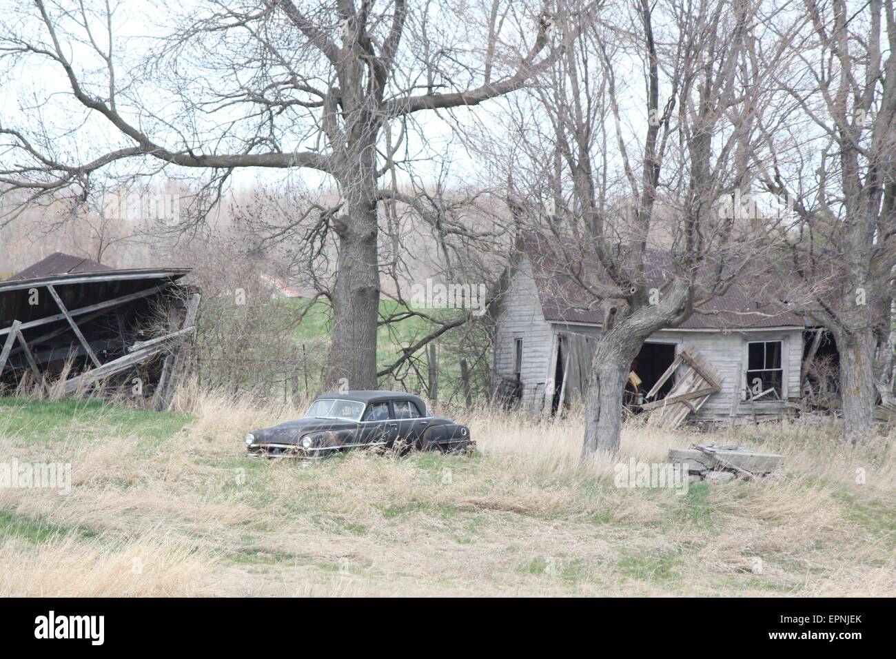 Old abandoned rural property with old rusting car, trees, and buildings ...