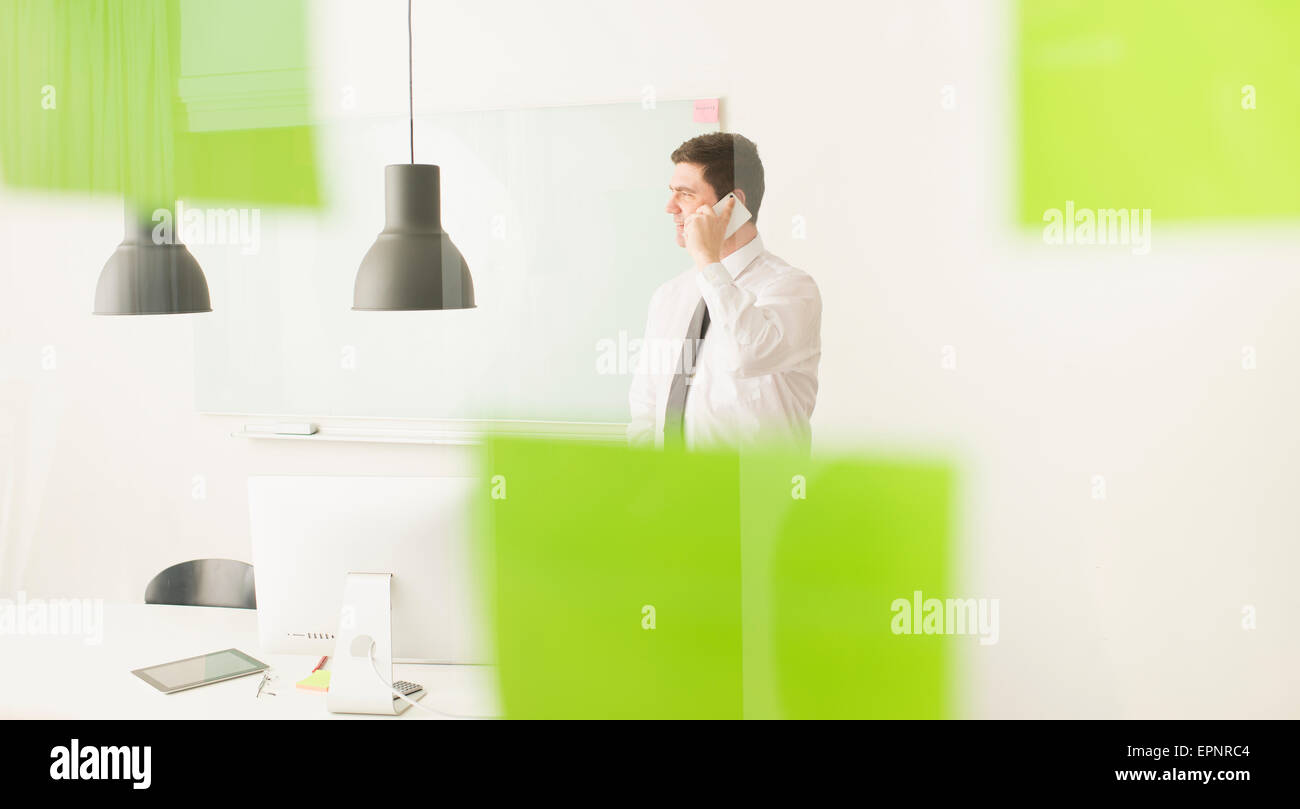 Businessman talking on cell phone behind glass wall with adhesive notes ...