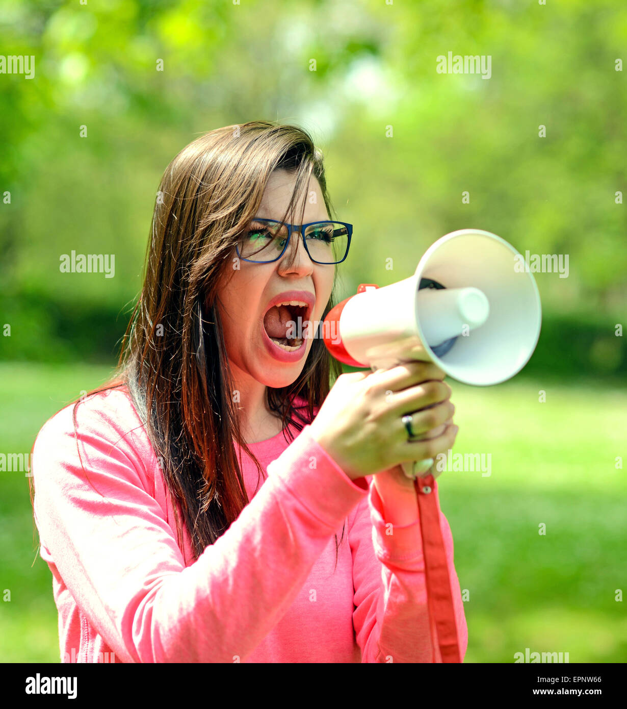 Portrait of middle aged woman shouting using megaphone against a nature ...