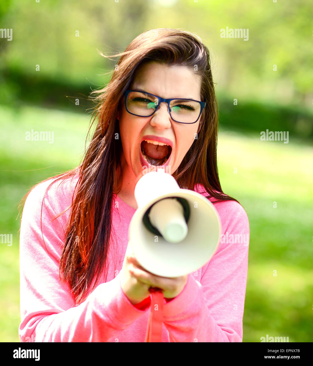 Portrait of middle aged woman shouting using megaphone against a nature ...