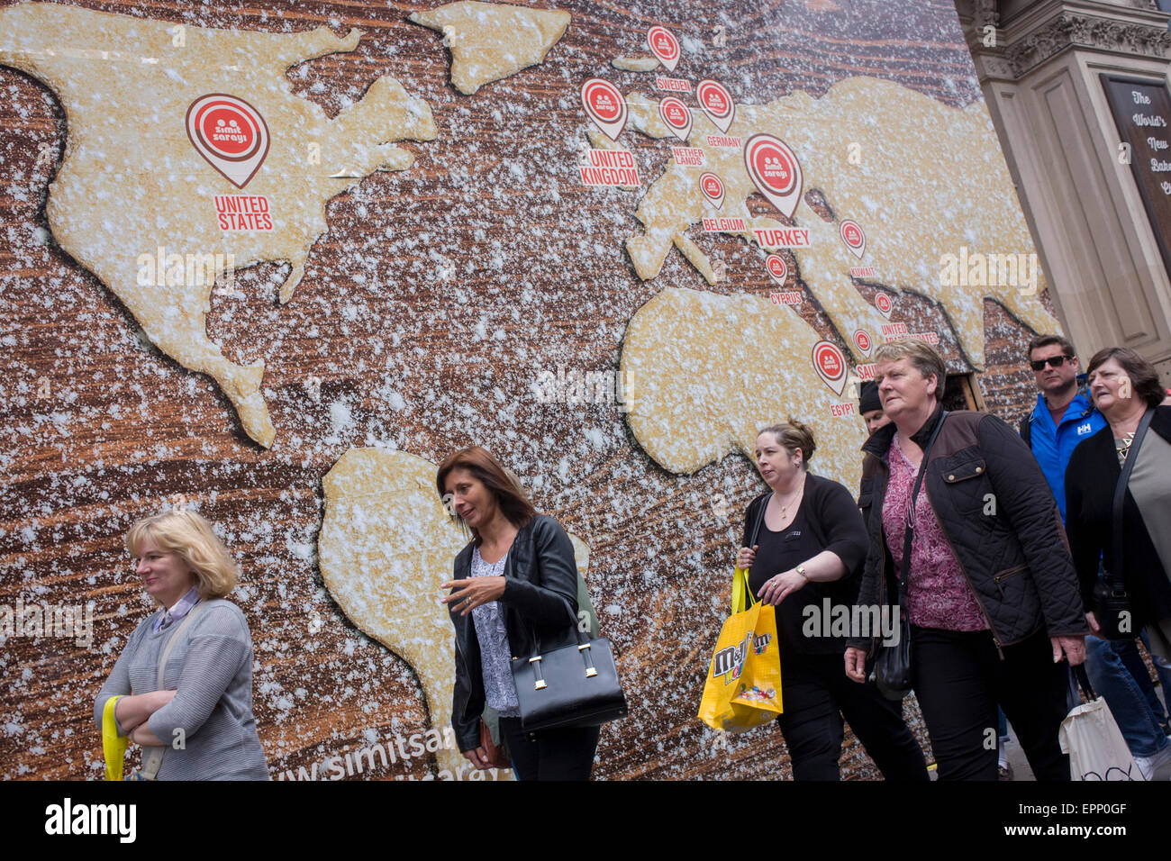 Shoppers walk beneath a world map on a bakery business hoarding Stock ...