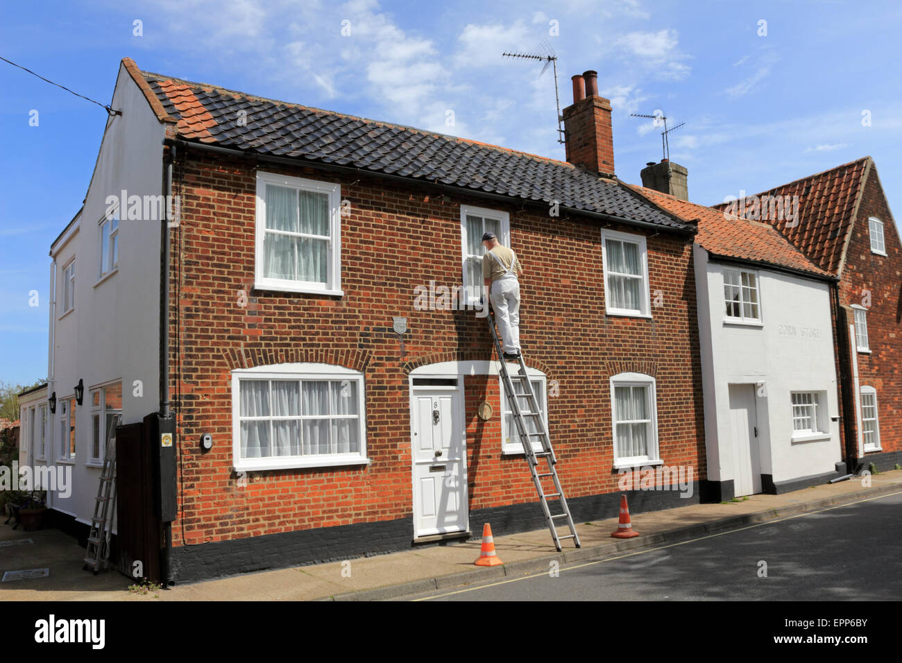 Man repairs first floor window up a ladder protected by cones, England ...