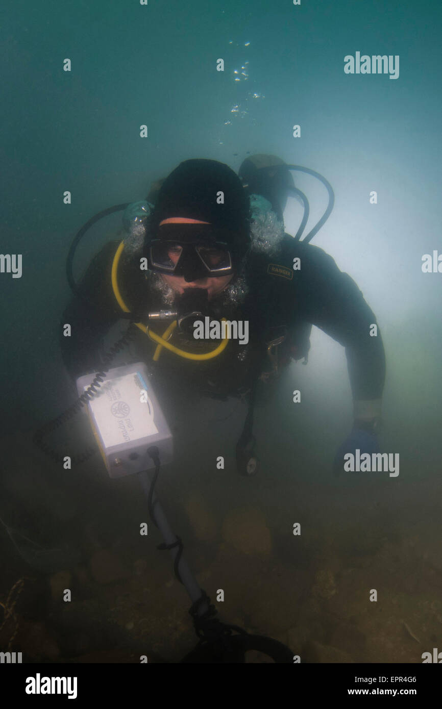 Underwater survey. Scuba diver uses a metal detector to help search for buried objects. In this ...