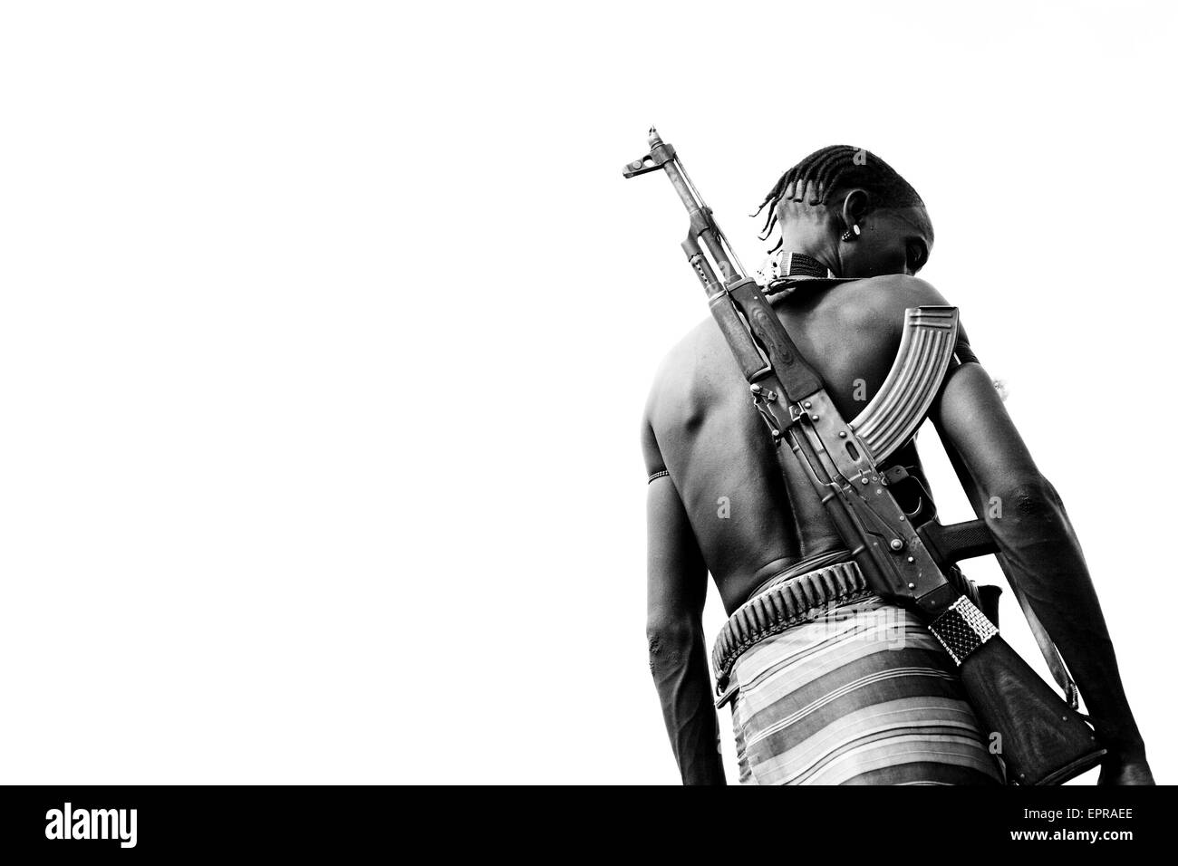 A man stands looking away from the camera with a kalashnikov rifle ...