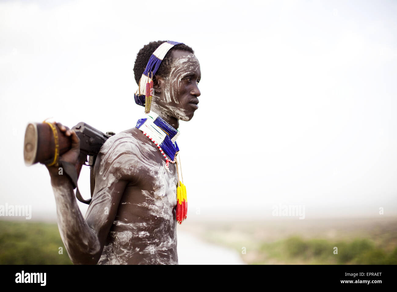 A young man holds his kalashnikov rifle while overlooking the Omo river ...