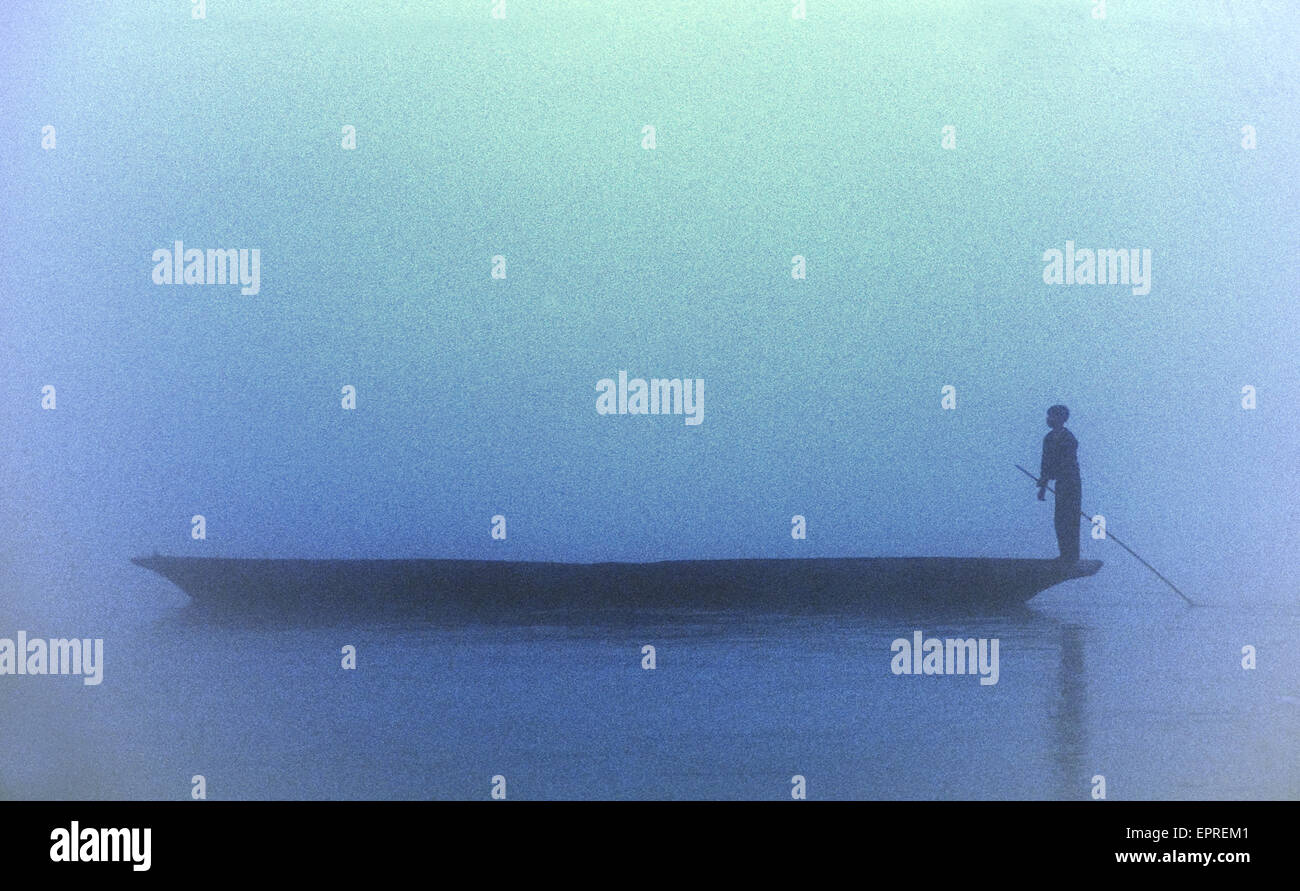 A boy stands in a dugout canoe crossing a river to ferry people in ...