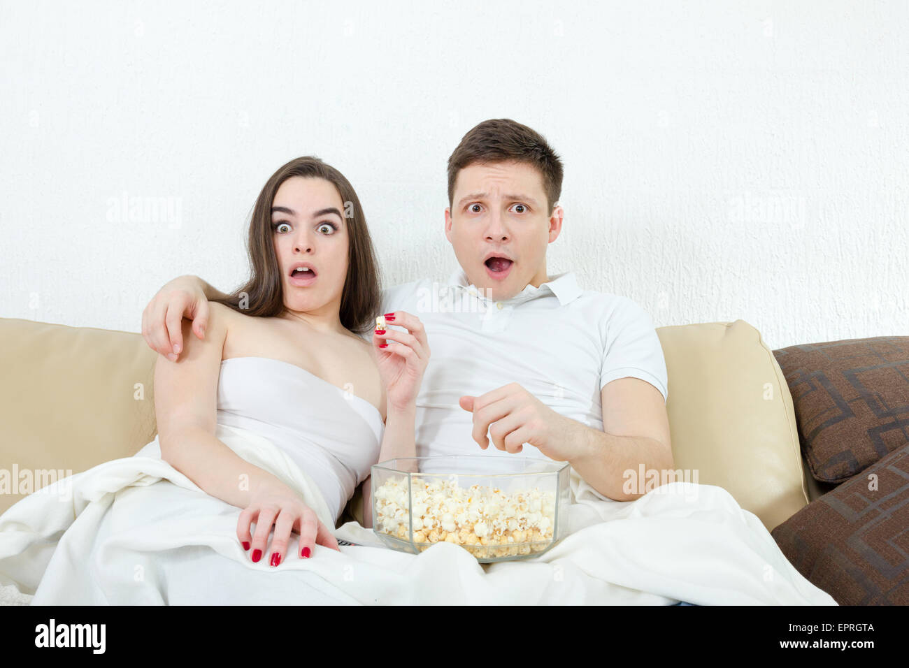 Frightened young attractive couple sitting on the couch in living room ...