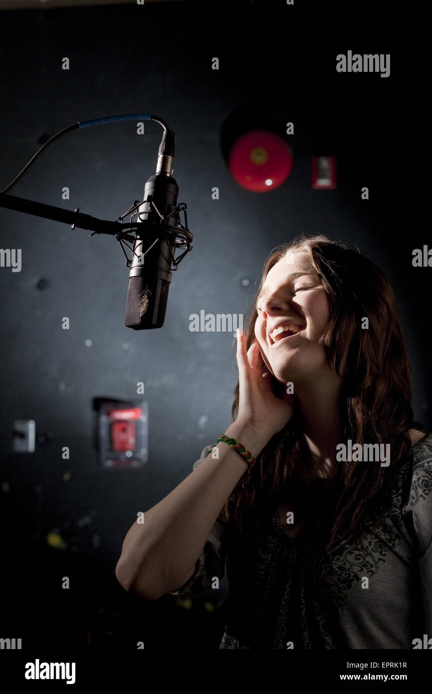 A female high school teenager (16) with hand to ear sings to microphone ...