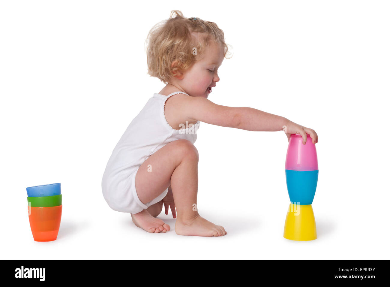 Two year old blond girl building a tower from coloured plastic cups on ...