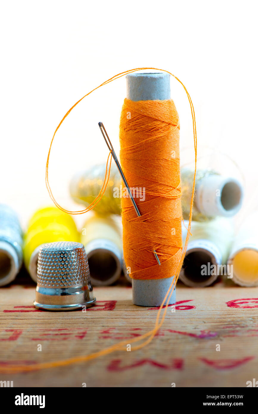 nedle with orange color thread and thimble on the white background ...