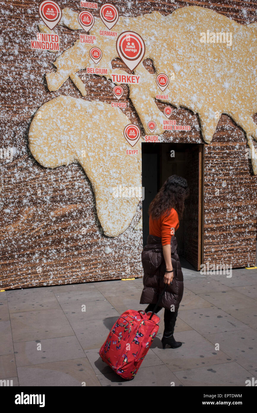 Tourist pulls baggage beneath a world map on a bakery business hoarding ...