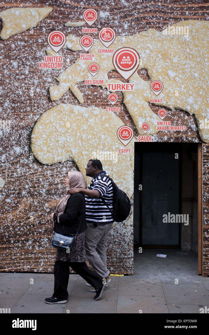 Muslim couple walk beneath a world map on a bakery business hoarding ...