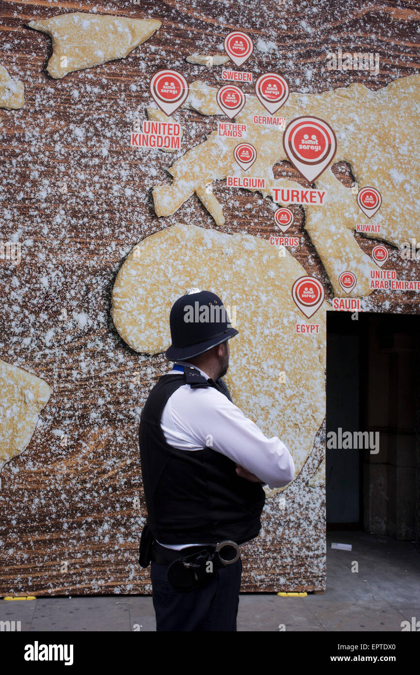 Police officer walks beneath a world map on a bakery business hoarding ...